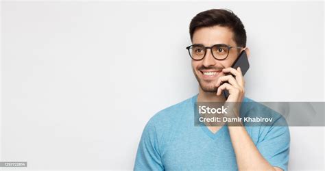 파란색 티셔츠를 입은 젊은 미소 짓는 남자의 수평 배너가 휴대 전화를 손에 들고 회색 배경에 고립 된 멀리 보고 있습니다 T 셔츠에 대한 스톡 사진 및 기타 이미지 Istock