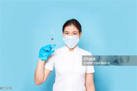 보호 마스크와 파란색 장갑을 낀 흰색 의료 용 코트를 입은 여성 의사 또는 간호사가 주사기를 손에 들고 파란색 배경에 고립 되어 있습니다 의학 및 의료의 개념 공간을