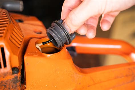 손으로 주황색 전기 톱으로 연료 혼합 탱크의 캡을 풉니 다 2 행정 엔진 클로즈업의 가솔린 용 가스 탱크 전기 톱에 연료 보급 Mandate에 대한 스톡 사진 및 기타