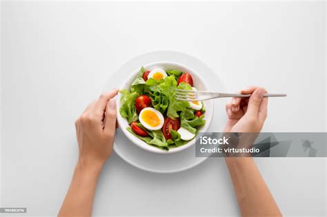 젊은 여자는 직접 위에서 본 흰 그릇에 신선한 샐러드 식사를 먹고 유기 야채와 포크를 들고 여성 손 간식 접시 위에서 본 최고의 볼 수 있습니다 상추에 대한 스톡 사진 및