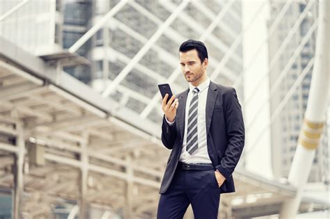 잘 생긴 젊은 사업가는 야외에 서서 스마트 폰을보고 휴대 전화를 사용하여 일상 생활에서 비즈니스를 제어 사물의 인터넷 Iot 비즈니스 개념 Brand Name Smart
