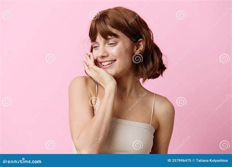 A Modest Shy Woman Stands On A Pink Background And Smiles Pleasantly With Her Eyes Closed And