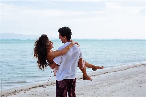 Man Carries A Girl In His Arms On The Beach By Stocksy Contributor