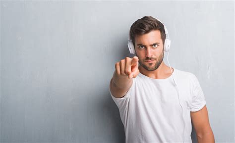 당신에 게 카메라를 손가락으로 가리키는 음악을 헤드폰을 착용 하는 회색 그런 지 벽에 잘생긴 젊은 남자 손 기호 정면에서 긍정적이 고 자신감 제스처 가리키기에 대한 스톡