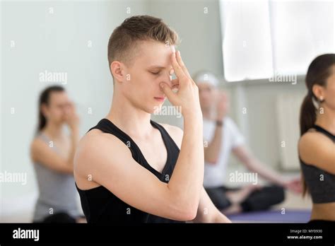 Young Man And Group Of Yogi People Practicing Yoga Lesson Doing Alternate Nostril Breathing