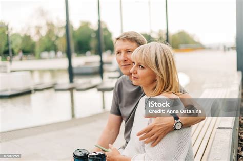 도시 거리 공원에서 야외 벤치에 앉아 사랑에 성인 성숙한 행복한 부부 금발의 백인 남자와 여자는 함께 시간을 보내고 커피를