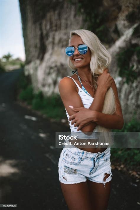 블루 안경 흰색 셔츠와 데님 반바지에 긴 금발 머리를 가진 아름 다운 여자는 발리에서 바위의 백 그 라에 포즈 건강한 생활방식에 대한 스톡 사진 및 기타 이미지 Istock