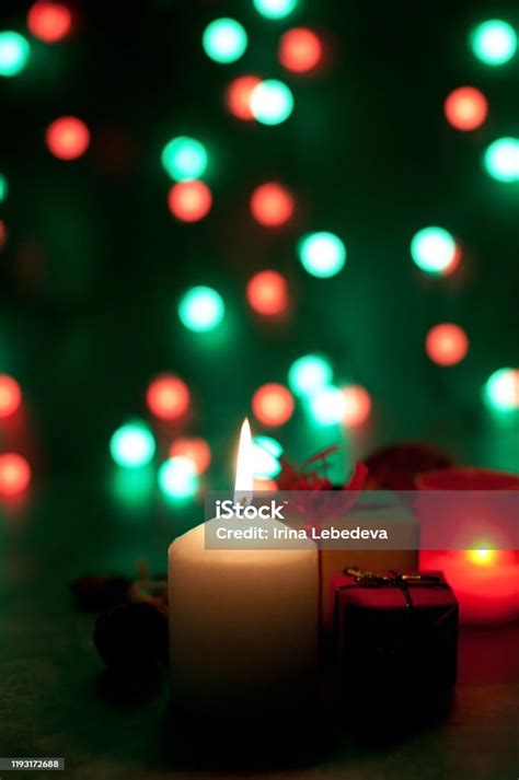 붉은색과 흰색 축제 촛불 공예 종이 등나무 공 계피 스틱과 여러 가지 색상의 크리스마스 화환의 배경에 아니스 별 중 테이블에 노란색 불꽃으로 구울 크리스마스 조명에 대한