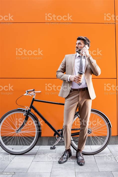 스마트폰으로 이야기하고 자전거 근처에서 종이 컵을 들고 오렌지 색 벽으로 건물을 짓는 사업가의 전체 길이 기업 비즈니스에 대한 스톡 사진 및 기타 이미지 Istock