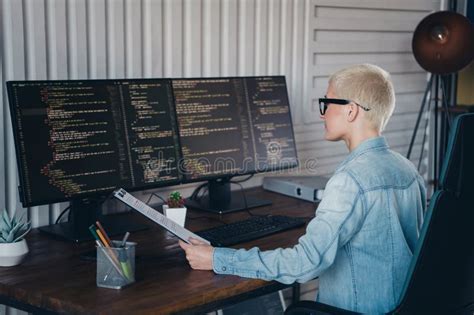 Young Female Programmer In Denim Shirt Working On Multiple Monitors Coding Software At Home