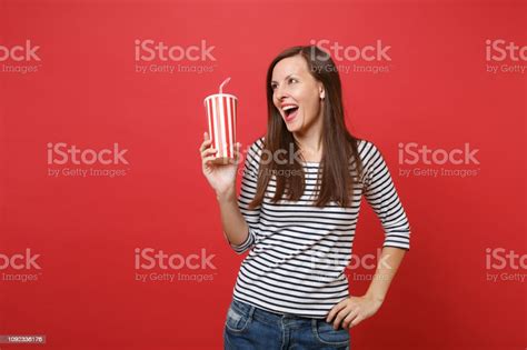 콜라 나 소 다 옆으로 보고의 쾌활 한 젊은 여 자가 지주 플라스틱 컵 밝은 빨간 벽 배경에 고립 입 벌리고 유지 사람들이 진심으 감정 라이프 스타일 개념 복사 공간을