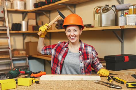 격자 무늬 셔츠에 백인 젊은 갈색 머리 여자를 꽤 회색 T셔츠 노란색 장갑 망치 나무 다른 도구 조각 나무 테이블 장소에 목공 워크숍에서 사용 하는 보호 헬멧 Diy에 대한