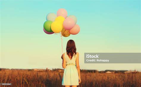 여름 밀짚모자를 쓰고 화려한 풍선을 잔뜩 쓴 젊은 여성의 뒷모습 야외에서 드레스를 입고 있다 25 29세에 대한 스톡 사진 및