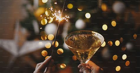 새해 복 많이 받으세요 크리스마스 트리 조명과 별의 배경에 불타는 폭죽과 샴페인 잔을 들고 있는 손 불꽃놀이 벵골 빛과 여자 손에 음료 대기 순간 사진
