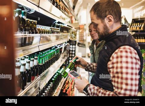 Man Using Bar Code Reader On Beer Bottle While Standing With Woman In Supermarket Stock Photo
