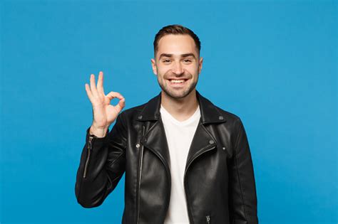 블랙 가죽 자 켓 흰색 T 셔츠에 잘생긴 세련 된 젊은 수염 남자 블루 벽 배경 스튜디오 초상화에 고립 된 카메라를 찾고 사람들은 진심으로 감정 라이프 스타일 개념입니다