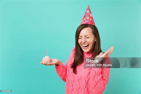 핑크 니트 스웨터에 젊은 여자를 웃 고 생일 모자와 함께 촛불 케이크 손에 잡고 확산 손을 유지 하는 눈을 감고 파란 배경에 고립 사람들의 라이프 스타일 개념입니다 복사