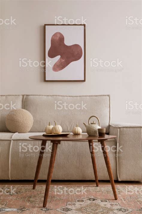 모의 포스터 프레임 베이지 색 소파 나무 커피 테이블 둥근 베개 무늬가있는 카펫 조각 및 개인 액세서리가있는 거실 인테리어의