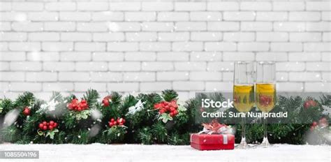 눈 덮인 테이블에 빨간 선물 상자 옆에 있는 설정 하는 두 샴페인 잔 장식 소나무 가지 붉은 홀리 열매 공간 상단 영역 흐린된 흰색 벽돌 벽 배경 복사 개념에 대한 스톡