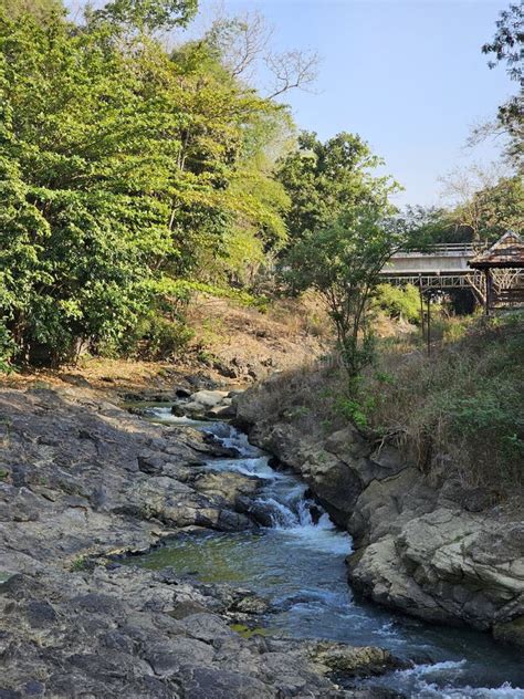A Scenic River Flows Through Lava Sediment Rocks With Trees Lining The Banks And A Bridge