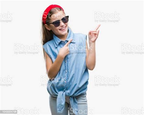 웃 고 옆에 두 손과 손가락으로 가리키는 카메라 보고 격리 된 배경 위에 선글라스를 입고 젊은 아름 다운 소녀 가리키기에 대한 스톡 사진 및 기타 이미지 Istock