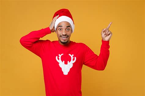 크리스마스 모자에 흥분 젊은 산타 아프리카 계 미국인 남자 가리키는 검지 손가락 에 모의 복사 공간에 노란색 배경에 고립 된 머리에 손을 넣어 새해 복 많은 연말연시 컨셉