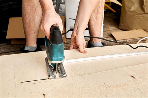 합판에서 전기 퍼즐로 부품을 톱질하고 절단하는 건설 노동자의 남성 손 절단 프로세스입니다 프렛소와 인테리어 장식의 Diy 건물