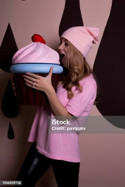 핑크 모자에 물결 모양의 머리와 아름다운 금발 모델 분홍색 배경에 큰 컵 케이크를 물고 휴일 컨셉 25 29세에 대한 스톡 사진 및 기타 이미지 Istock