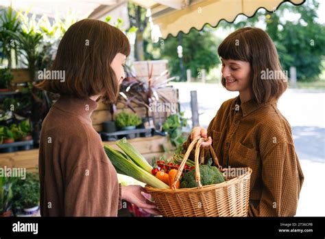 Smiling Twin Sisters Holding Basket Of Vegetables At Farmers Market