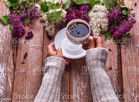 손은 위에서 나무 배경보기에 꽃이 피는 봄 라일락 꽃 가지가있는 모닝 커피 한 잔을 보유하고 있습니다 플랫 레이 지하 스타일 비싼 색상 꽃의 창조적 인 디자인 꽃 나무에