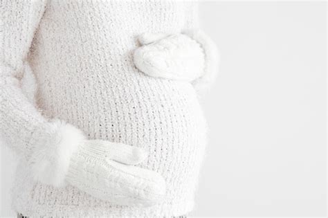 장갑에 손으로 큰 배를 만지는 흰색 푹신한 스웨터에 임신 한 여성 회색 배경에 격리되었습니다 임신 시간에 추운 날씨에 따뜻한 옷 아기 기대 측면 뷰 근접 촬영 겨울에 대한