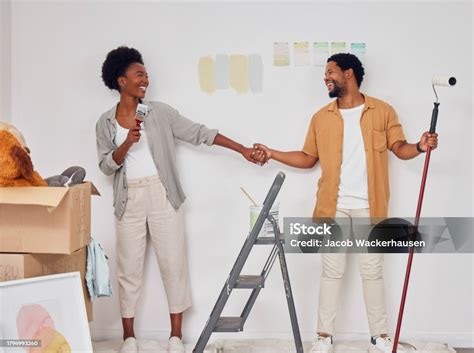 그림을 그리거나 손을 잡거나 Diy로 노래하는 흑인 커플 붓으로 집 개조 또는 리모델링 놀고 미소 또는 재미있는 아프리카 남자는 팀워크로 집에서 춤추는 행복한 여자와 웃고
