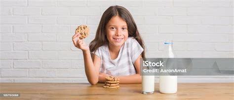 젊은 라틴계 아이 우유를 마시는 서 치아를 보여주는 자신감 미소로 웃 고 행복 한 얼굴로 초콜릿 쿠키를 먹는 테이블에 앉아 긍정적인 감정 표현에 대한 스톡 사진 및 기타