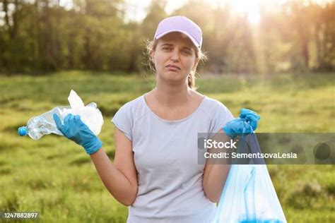 현장에서 쓰레기를 줍고 아무렇지 않게 입고 쓰레기 봉투를 들고 피곤하고 화가 난 표정으로 카메라를 바라보며 공원 전체를 청소하고 환경 문제를 해결합니다 가방에 대한 스톡