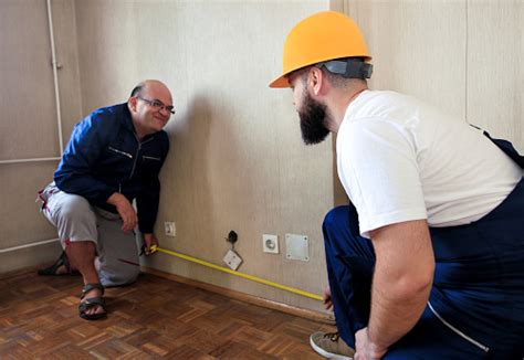 엔지니어 계약자 및 프로젝트 관리자는 동료 건설 노동자 핸디맨 및 빌더와 함께 건설 현장에서 측정 테이프를 사용하여 리노베이션을 위해 아파트의 벽실을 측정하고 있습니다 2
