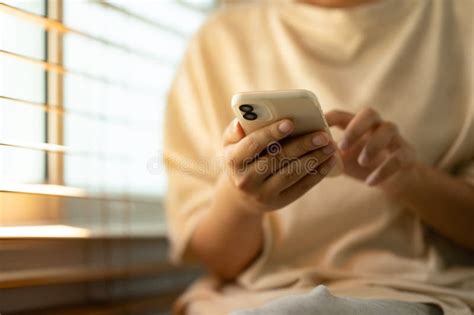 Close Up Of A Woman Using Smartphone Sitting Near A Window With Wooden Blinds Stock Image