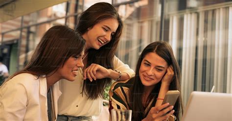 세 명의 젊은 여성이 카페에 앉아 스마트폰을 사용하여 재미있는 대화를 나눴다 그들 중 한 명이 시계로 지켜보고 있습니다 사진 Unsplash의 청년 성인 이미지