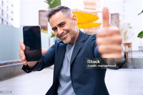 남자는 스마트 폰을 들고 야외에서 엄지 손가락을 올리는 제스처를 제공합니다 Brand Name Smart Phone에 대한 스톡 사진 및 기타 이미지 Brand Name