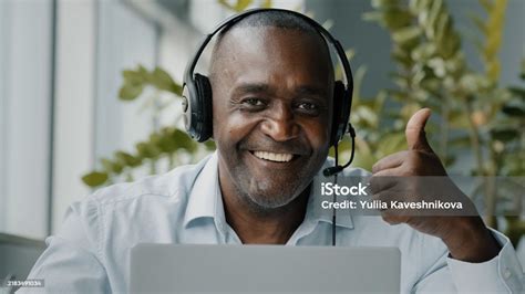 고위 아프리카 직원 사무실 책상에 앉기 마이크가 달린 헤드폰 착용 노트북에서 화상 회의에 연결 비즈니스 통화 웹캠으로 의사 소통 온라인 채팅에서 대화 엄지 손가락을