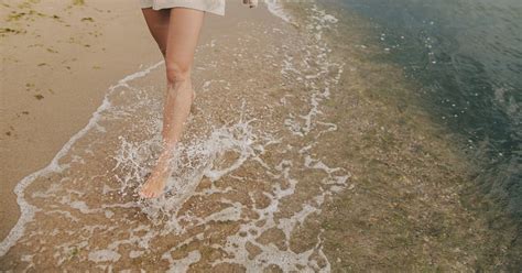 튀는 파도에 발 차가운 바다 파도와 함께 맨발로 모래 사장을 달리며 즐거운 시간을 보내는 평온한 아름다운 여성 잘린 보기 해안에서 휴식을 취하고 휴가를 즐기는 세련된