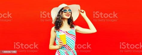 빨간 배경에 여름 모자를 쓰고 멀리 바라보는 주스 한 잔을 들고 행복한 미소 짓는 젊은 여성의 초상화 광고 텍스트를위한 빈 복사