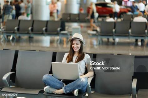 젊은 여행자 관광 여자 모자 교차 다리 노트북에 앉아 웃 고 국제 공항의 로비 홀에서 대기 주말도 주에 해외 여행 하는 승객 공기 비행 개념입니다 건축에 대한 스톡 사진 및