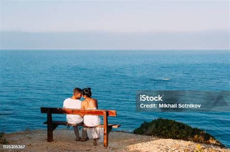 일몰에 사랑에 빠진 커플입니다 새벽에 남녀 부부는 바다에 의해 벤치에 앉아입니다 바다에서 키스 하는 커플 허니문 여행입니다 바다에 일몰입니다 새벽 바다입니다 결혼식 여행 해
