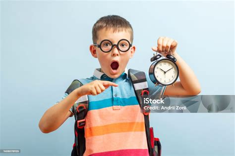 배낭을 든 안경을 쓴 충격을 받은 여학생은 손에 알람 시계를 들고 파란색 배경에 손가락으로 가리켰다 일정과 타이밍 학교로 돌아가기 신학기에 대한 스톡 사진 및 기타 이미지