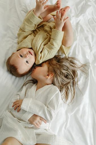 Girls Sisters In Bathrobes Lie In Bed The Older One Kisses The Younger