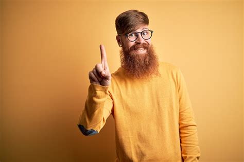 성공적인 아이디어와 손가락을 가리키는 노란색 고립 된 배경 위에 안경을 쓰고 수염을 가진 잘 생긴 아일랜드 빨강 머리 남자 종료하고 행복 넘버 원 가리키기에 대한 스톡 사진