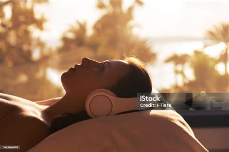 불면증 헤드폰을 끼고 침대에 베개에 누워 잠을 잘 수 없는 여자의 실루엣 파노라마 창문이 있는 침실과 일몰 일출의 야자수 바다 해변의 전망 헤드폰에 대한 스톡 사진 및 기타