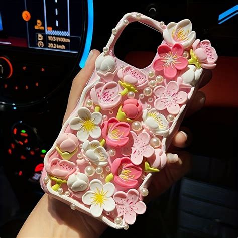 A Hand Holding A Pink Phone Case With Flowers And Leaves On The Back In Front Of A Steering Wheel