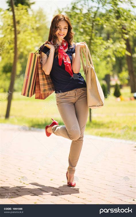 زن جوان زیبا در پارک ایستاده و کیسه های خرید را در دست دارد 1091598