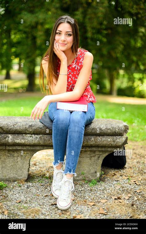 Beautiful Female College Sitting On A Bench In The Park And Holding A